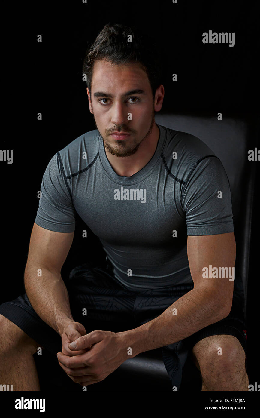 Low key studio portrait of muscular young man sat in gym shirt and ...