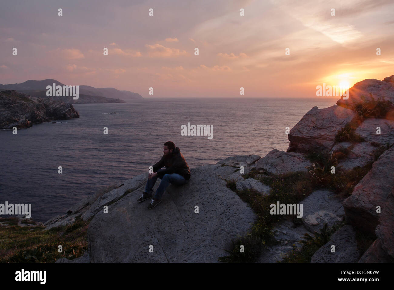 Young man with his back turned to the sunset view, sitting on a high ...