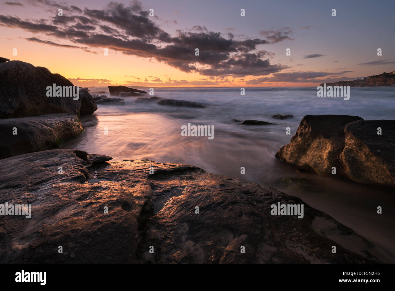 Seascape sunrise long exposure with flowing water around large rocks ...