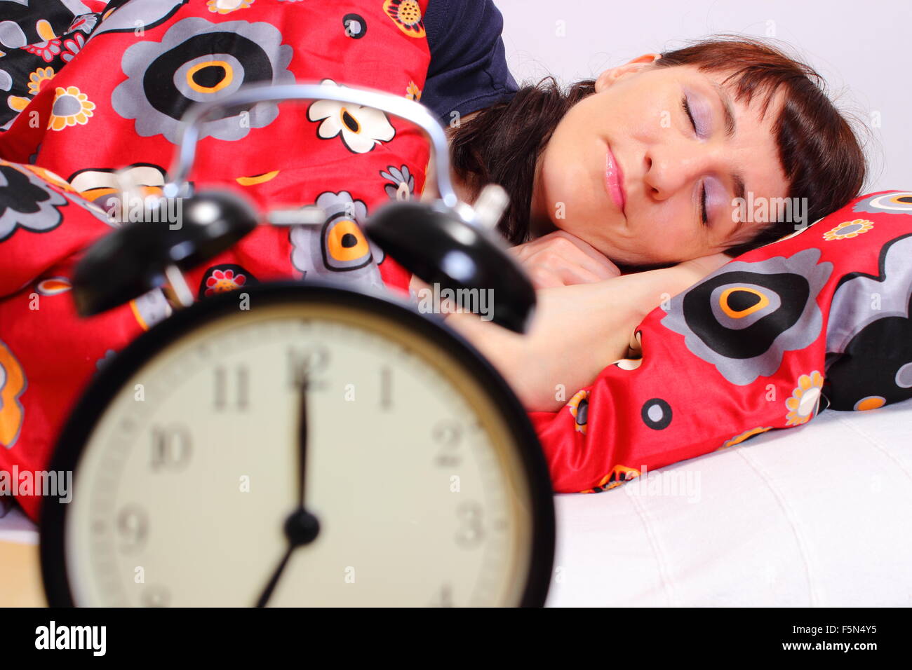 Beautiful woman sleeping on bed in her bedroom and ringing alarm clock ...