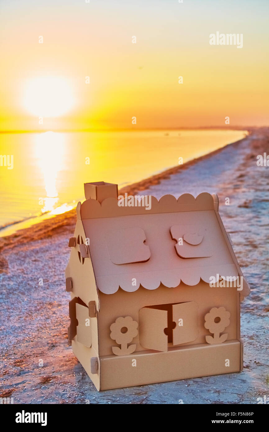 Toy house made of corrugated cardboard in the sea coast at sunset. The ...