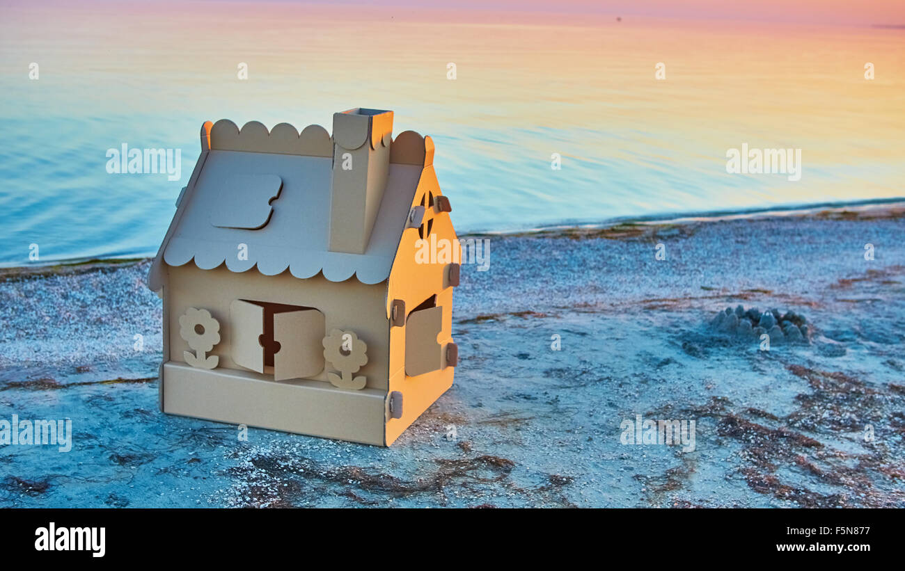Toy house made of corrugated cardboard in the sea coast at sunset. The ...