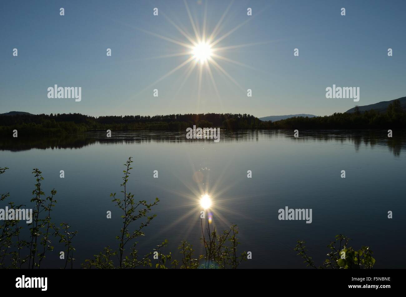 bright sun on blue summer sky with clear reflection on calm summer ...