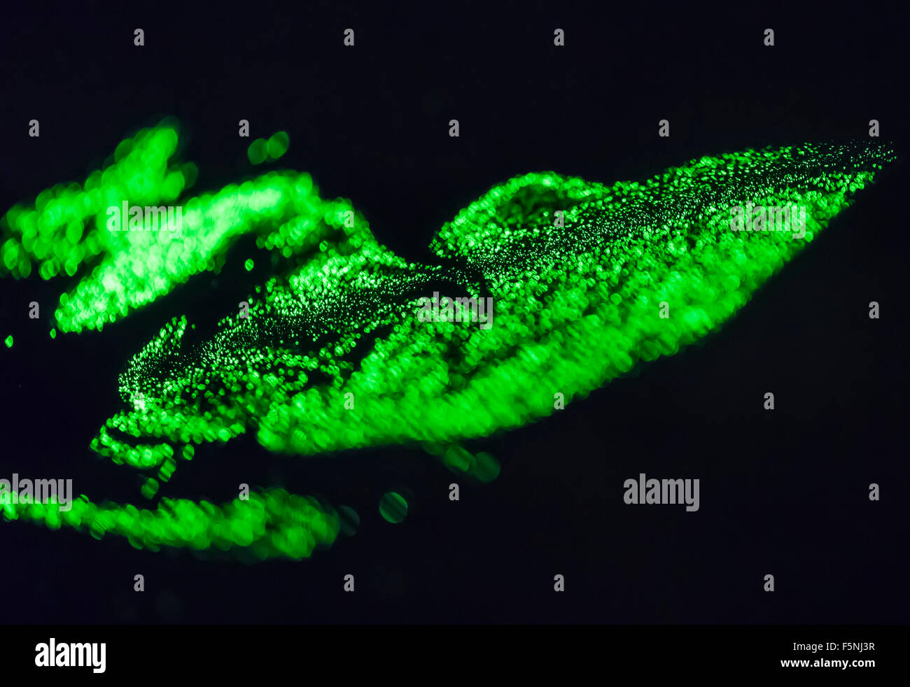 Cloud of bright green dust particles floating in air and illuminated by ...