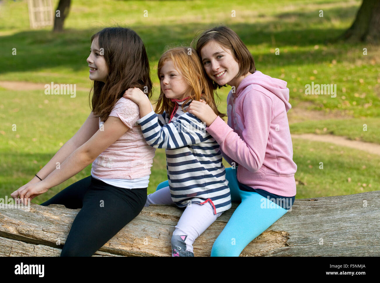 Three young girls sit astride a log playing pretend. The are obviously ...
