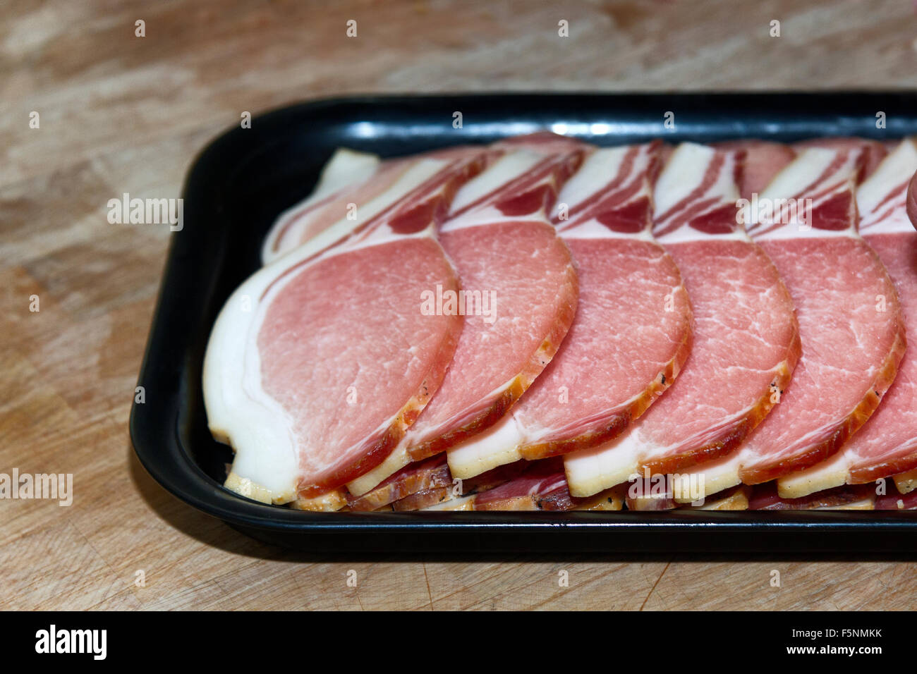 Rashers of back bacon in a plastic tray on a wooden block Stock Photo ...