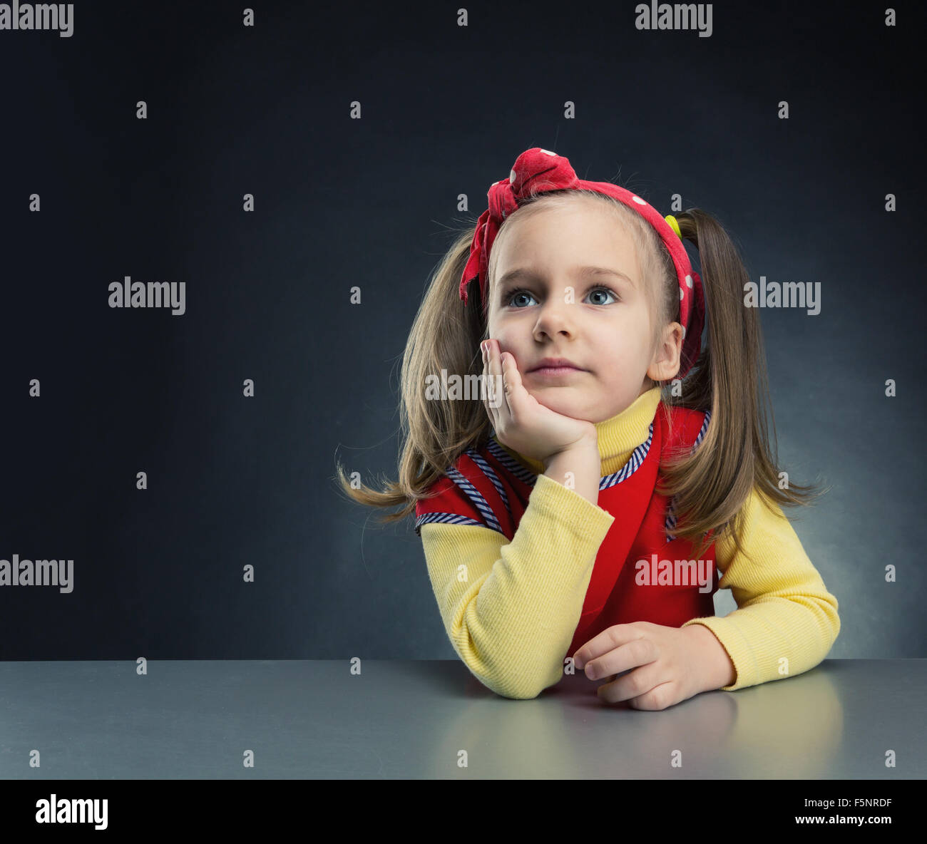 Cute little girl thinks with her hand under chin over grey Stock Photo ...