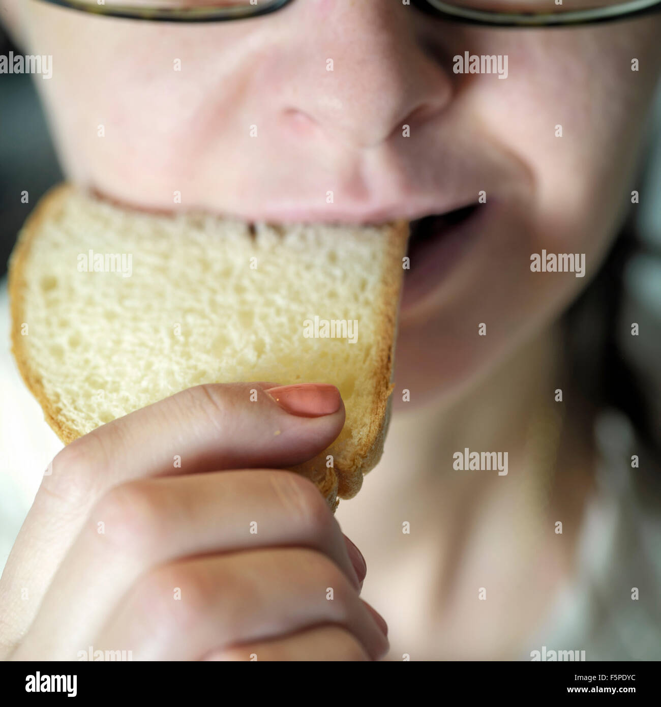 Woman biting bread, indoor square shot with shallow depth of field ...