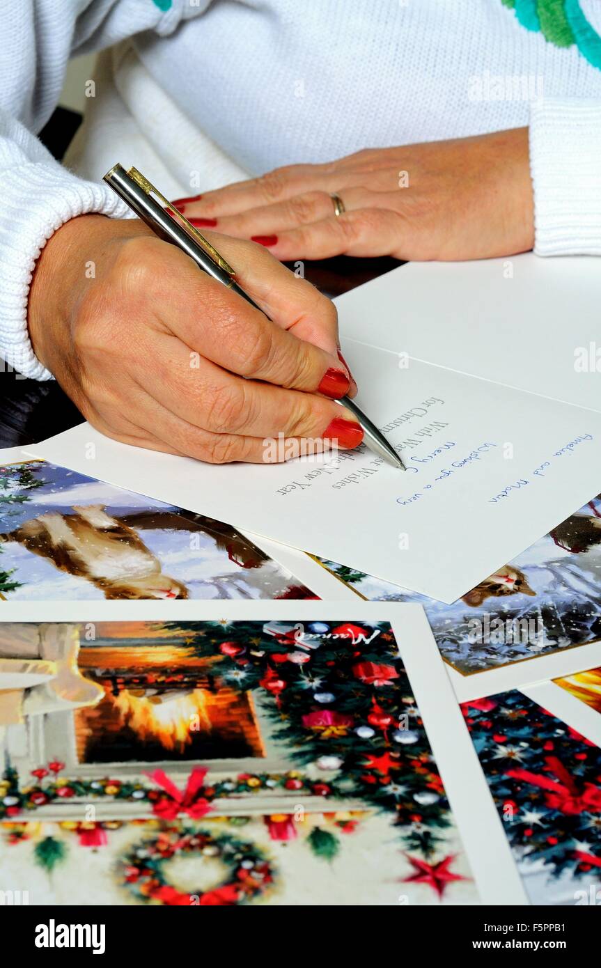 Woman writing Christmas cards with cards scattered around the table ...
