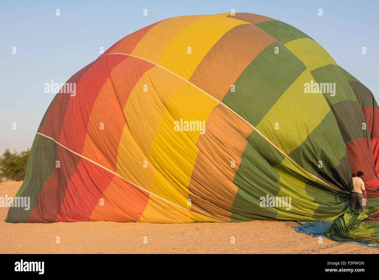 Multi-colored hot air balloon being deflated after landed on a desert ...