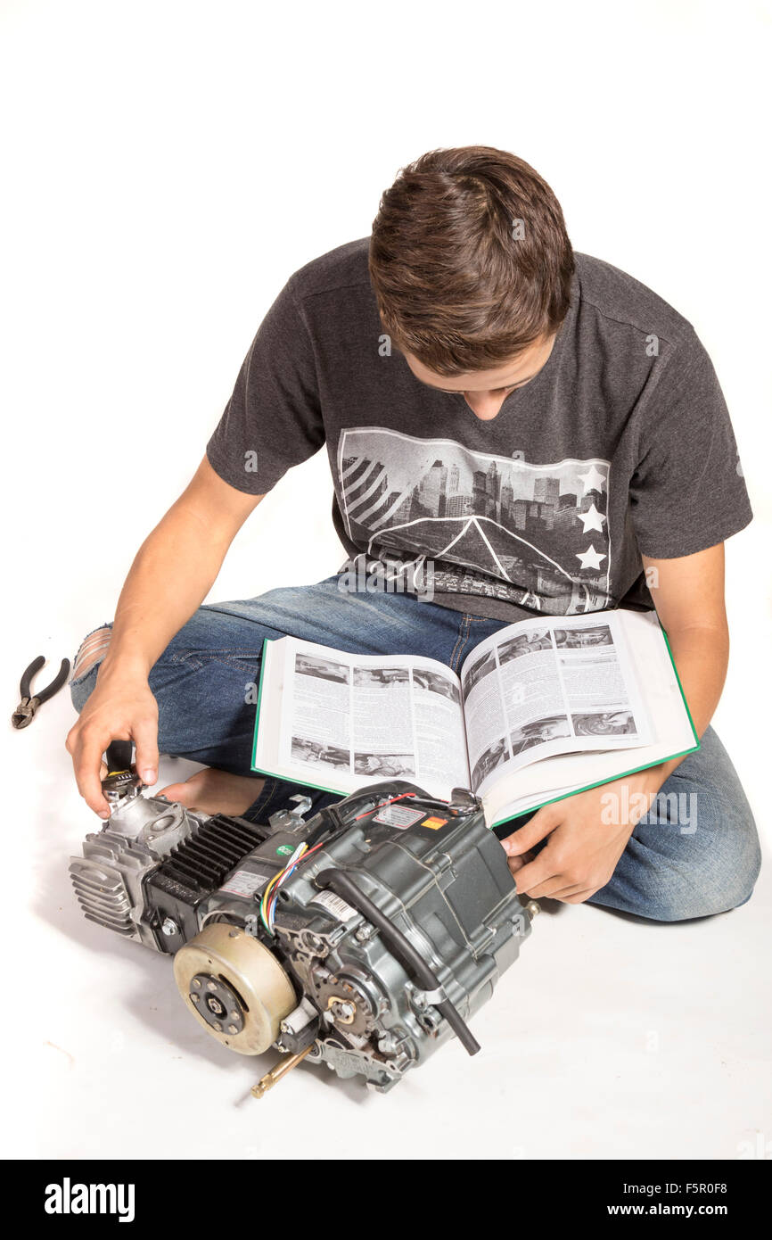 Teenage boy fixing an engine while reading a manual Stock Photo - Alamy