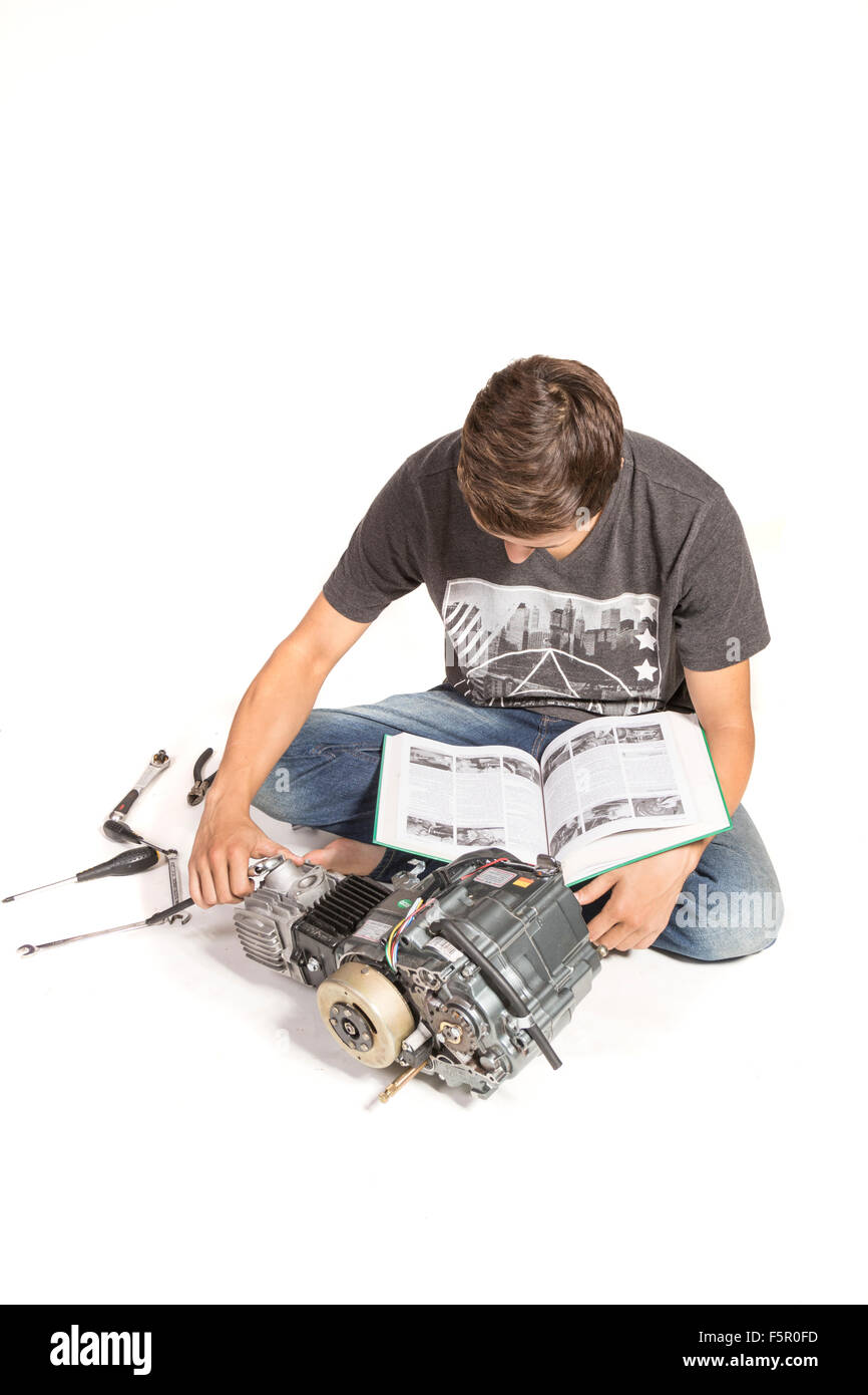 Teenage boy fixing an engine while reading a manual Stock Photo - Alamy