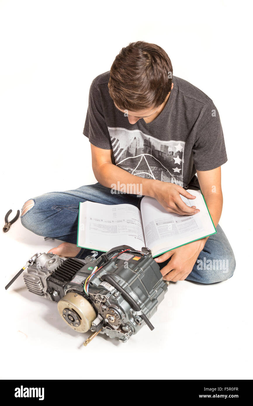 Teenage boy fixing an engine while reading a manual Stock Photo - Alamy