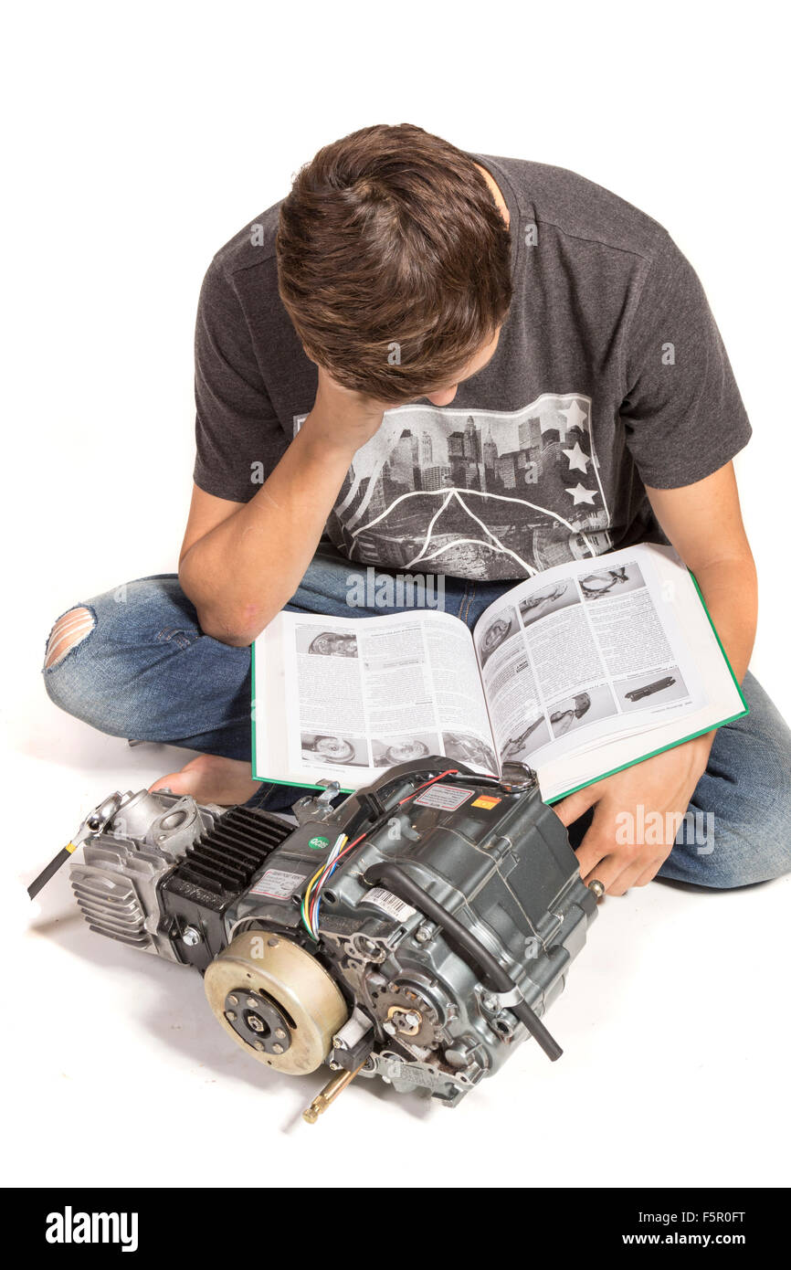 Teenage boy fixing an engine while reading a manual Stock Photo - Alamy
