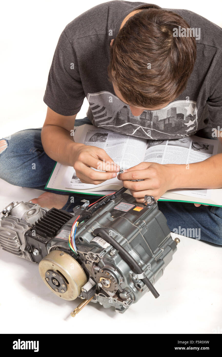 Teenage boy fixing an engine while reading a manual Stock Photo - Alamy