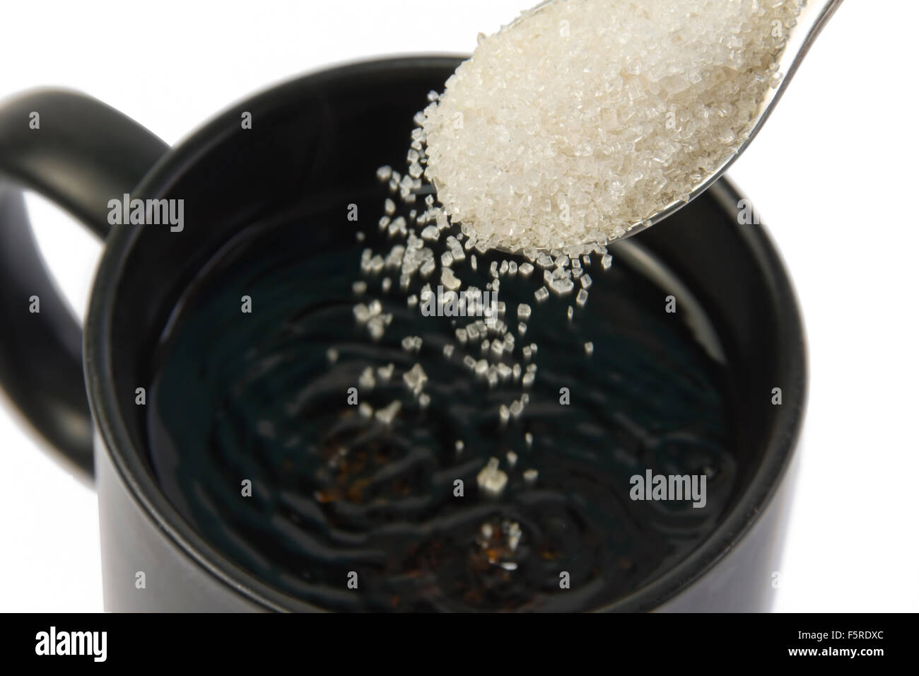White sugar falling from spoon into a cup isolated on white background ...
