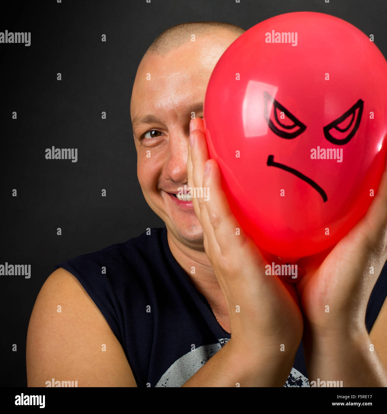 Happy man hiding behind red balloon with angry smiley Stock Photo - Alamy