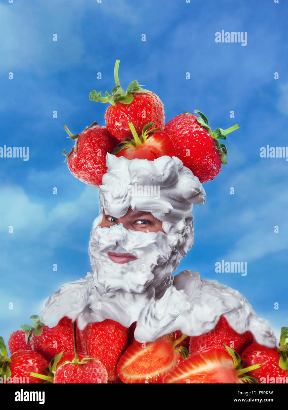 Smiling man with whipped cream and strawberries on his head over sky ...