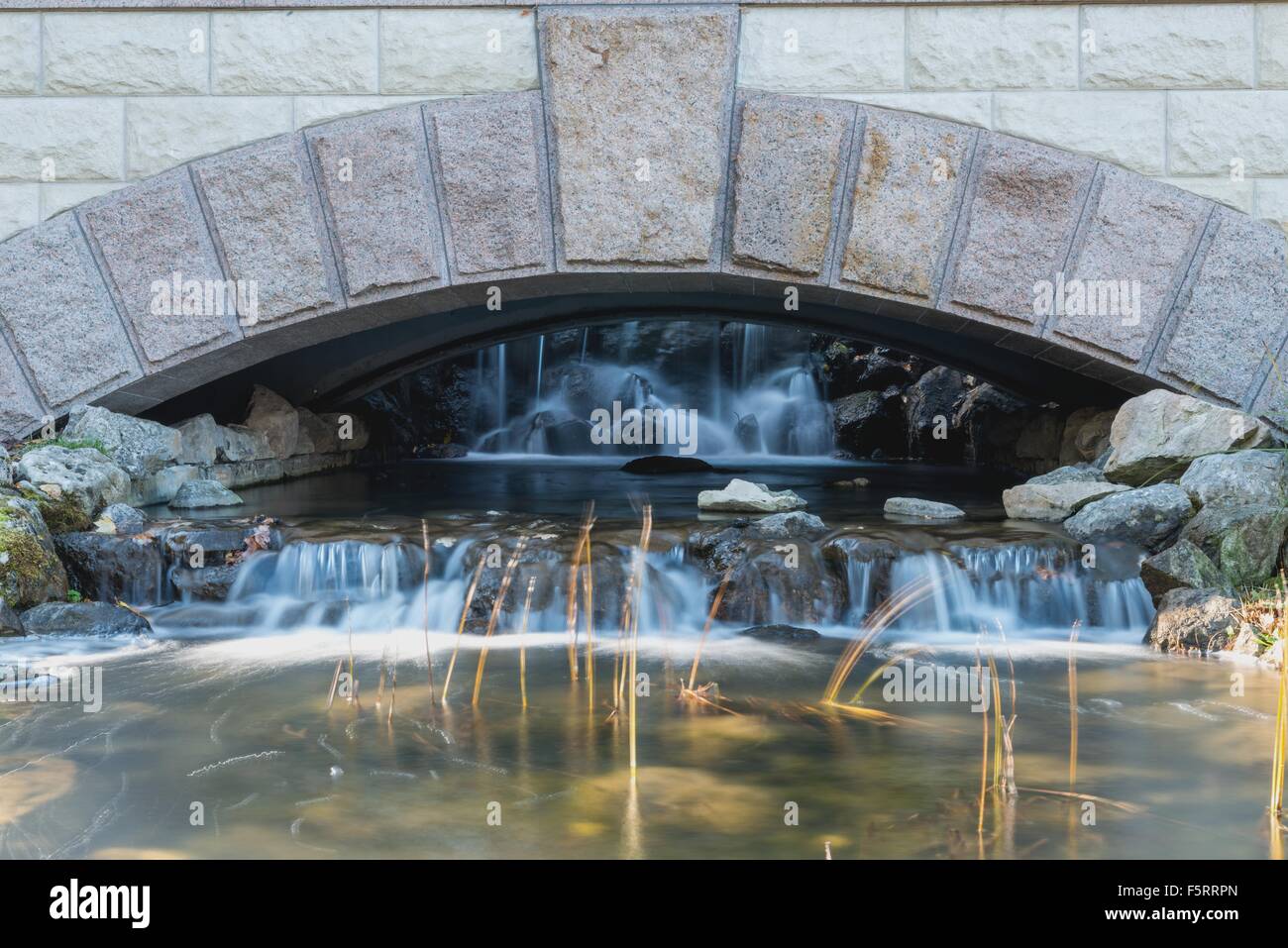 A small waterfall under a bridge Stock Photo - Alamy