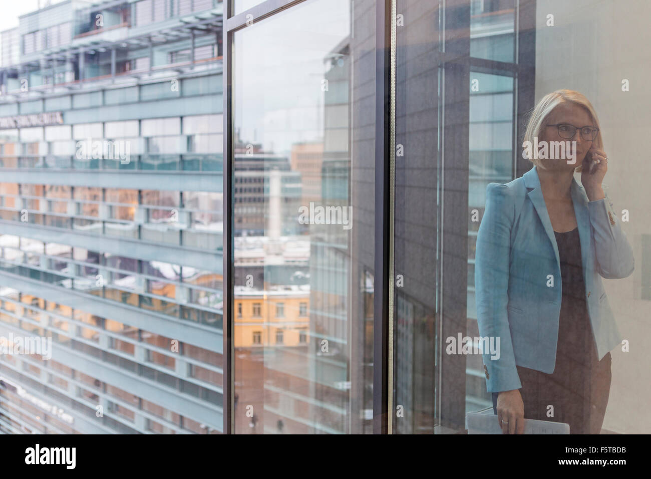 Finland, Helsinki, Businesswoman seeing through window talking by phone ...