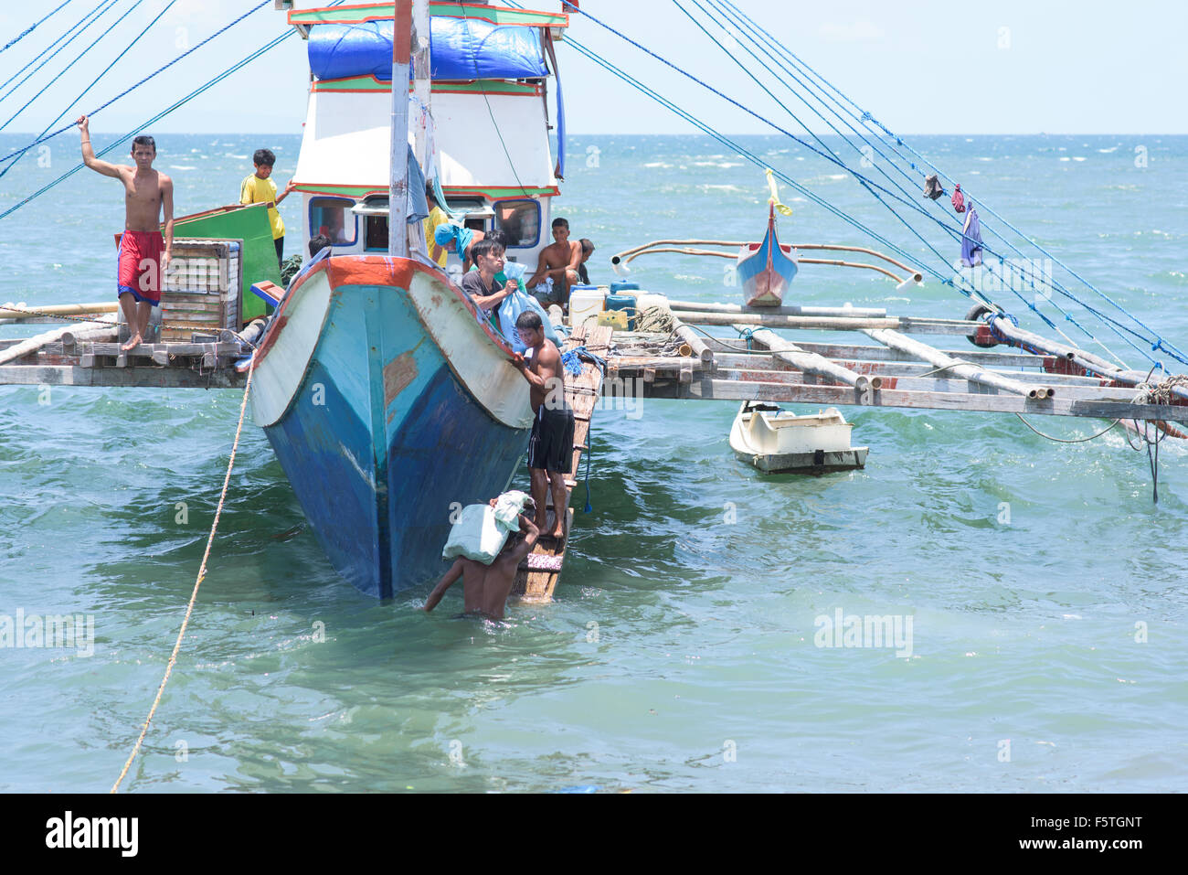 Workers carrying goods onto a small cargo vessel with outriggers at ...