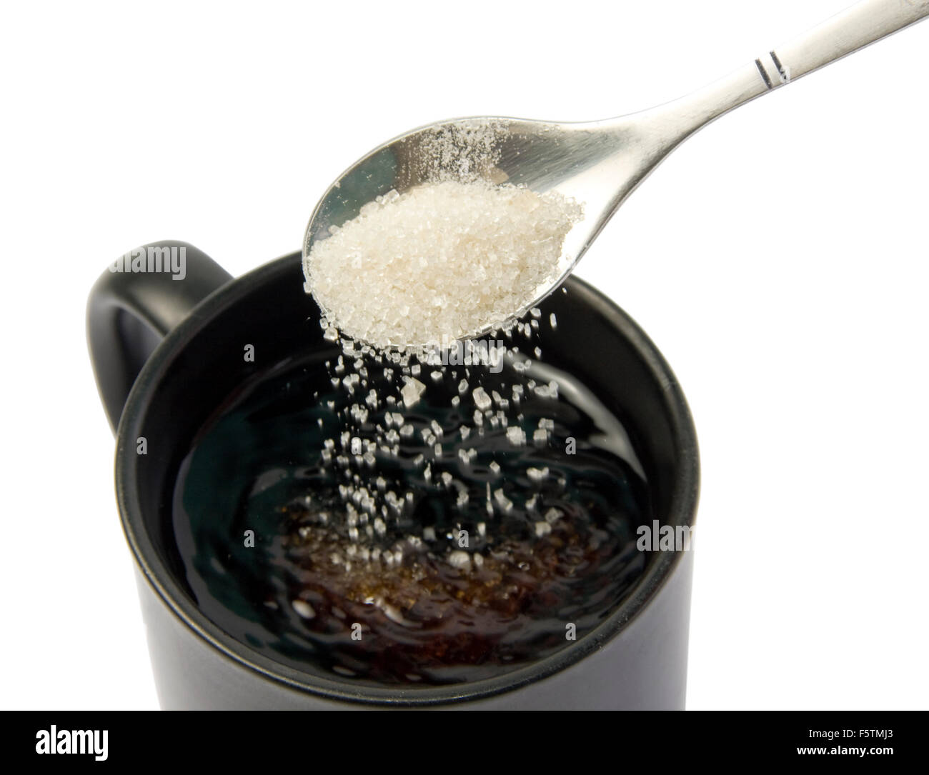 White sugar falling from spoon into a cup isolated on white background ...