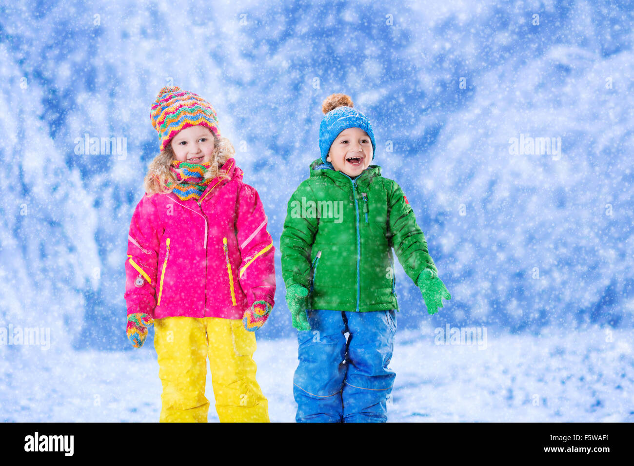 Little girl and boy in colorful hat catching snowflakes in winter park ...