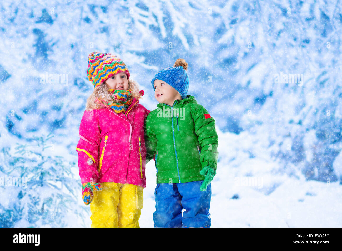 Little girl and boy in colorful hat catching snowflakes in winter park ...