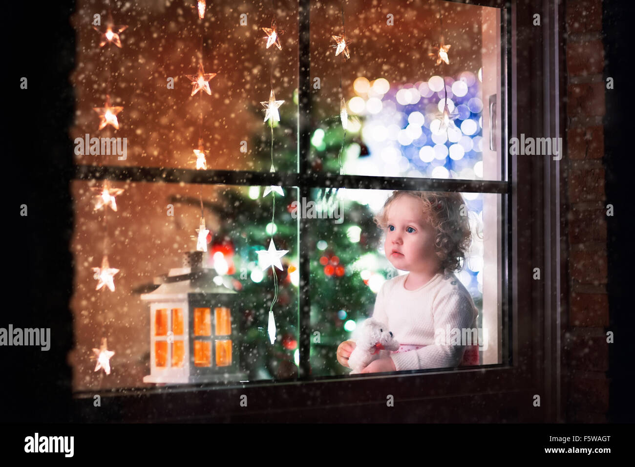 Little girl watching snow through window. Family with children on ...