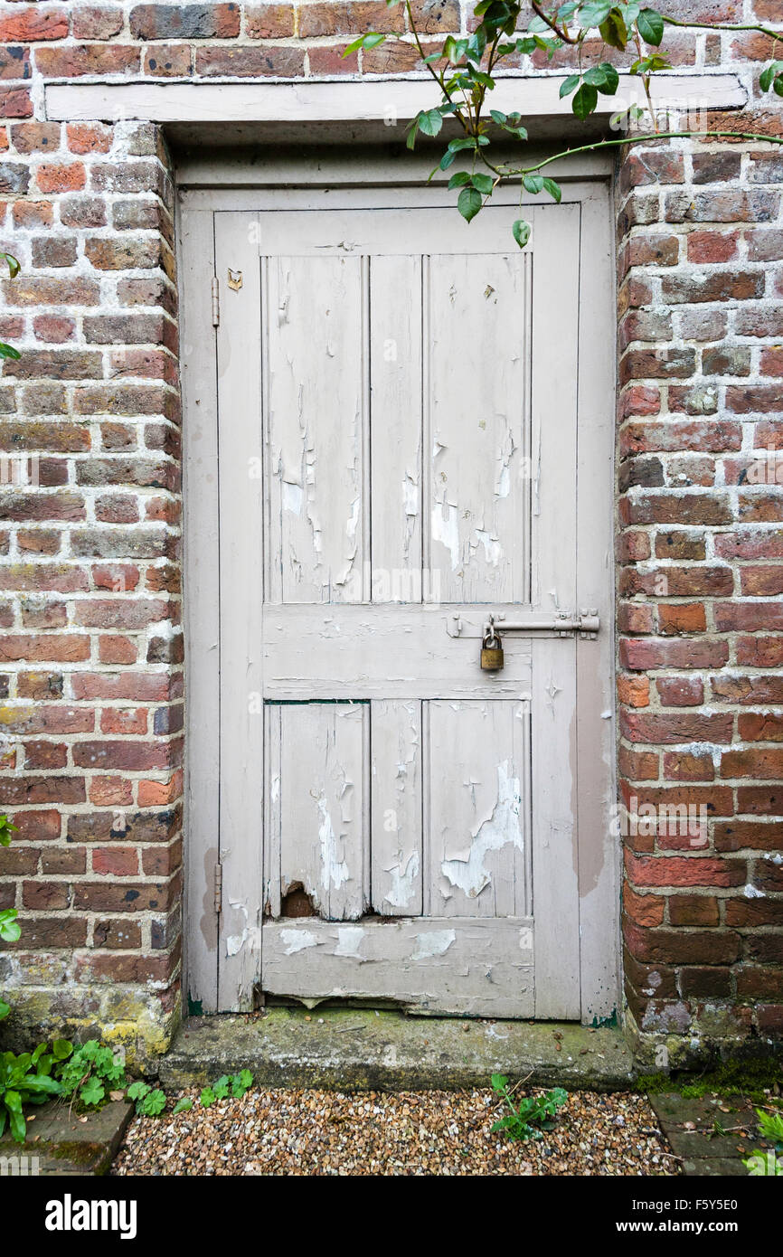 England. Old battered grey panelled exterior door and frame in brick ...