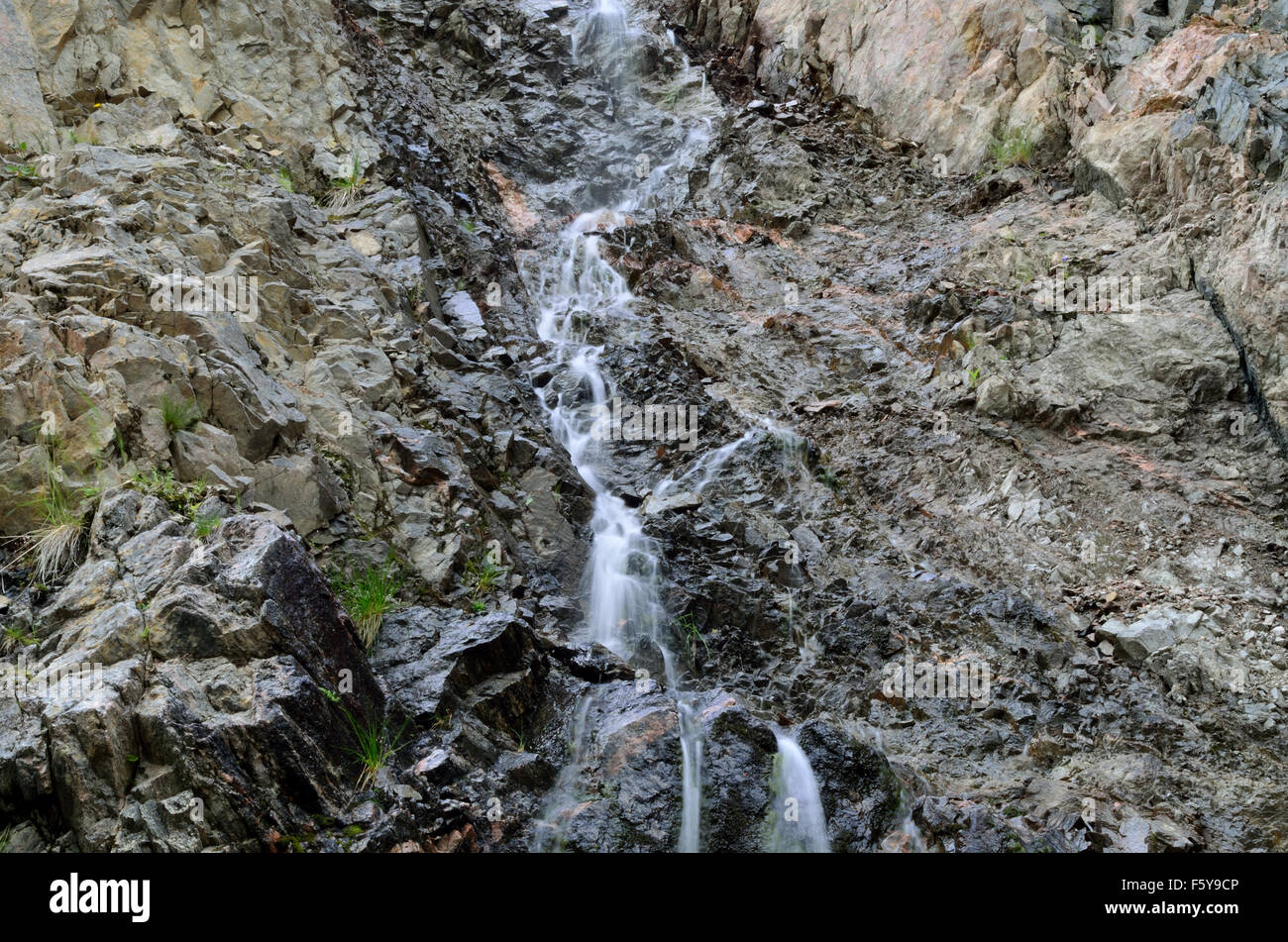 beautiful small mountain waterfall running down colorful and jagged ...
