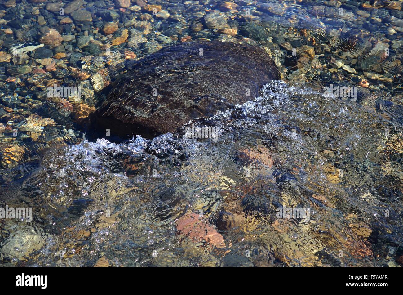 cold river water stream hit a black river rock in summer sunshine Stock ...