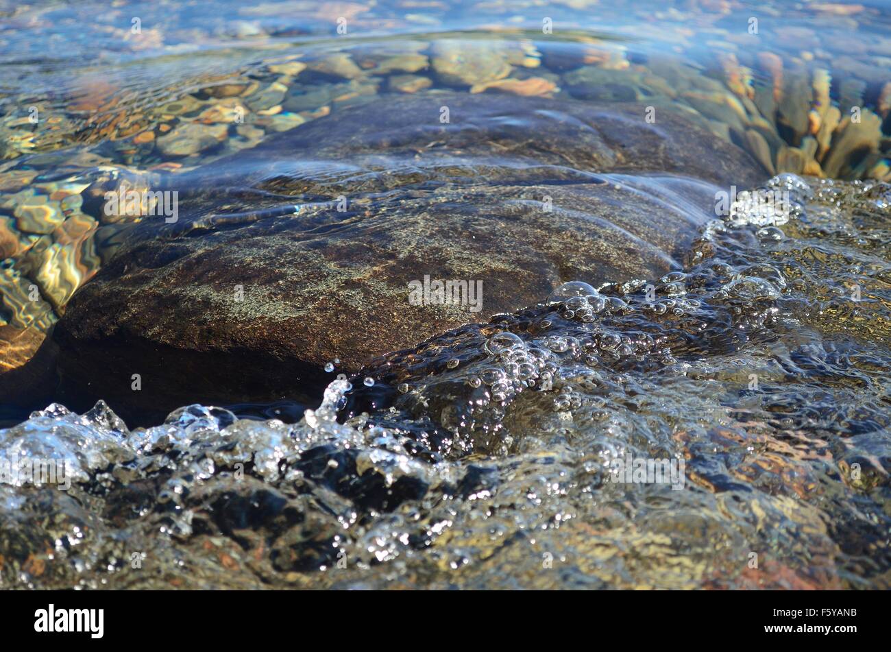 cold river water stream hit a black river rock in summer sunshine Stock ...