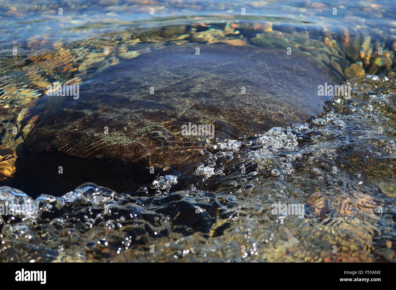 cold river water stream hit a black river rock in summer sunshine Stock ...