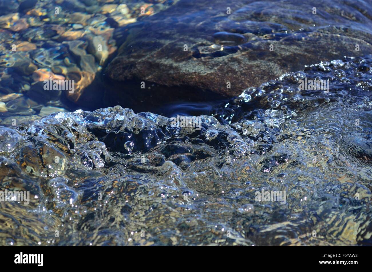 cold river water stream hit a black river rock in summer sunshine Stock ...