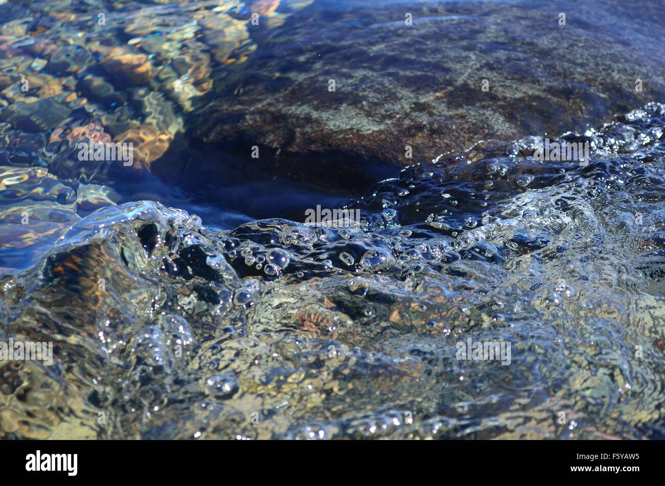 cold river water stream hit a black river rock in summer sunshine Stock ...