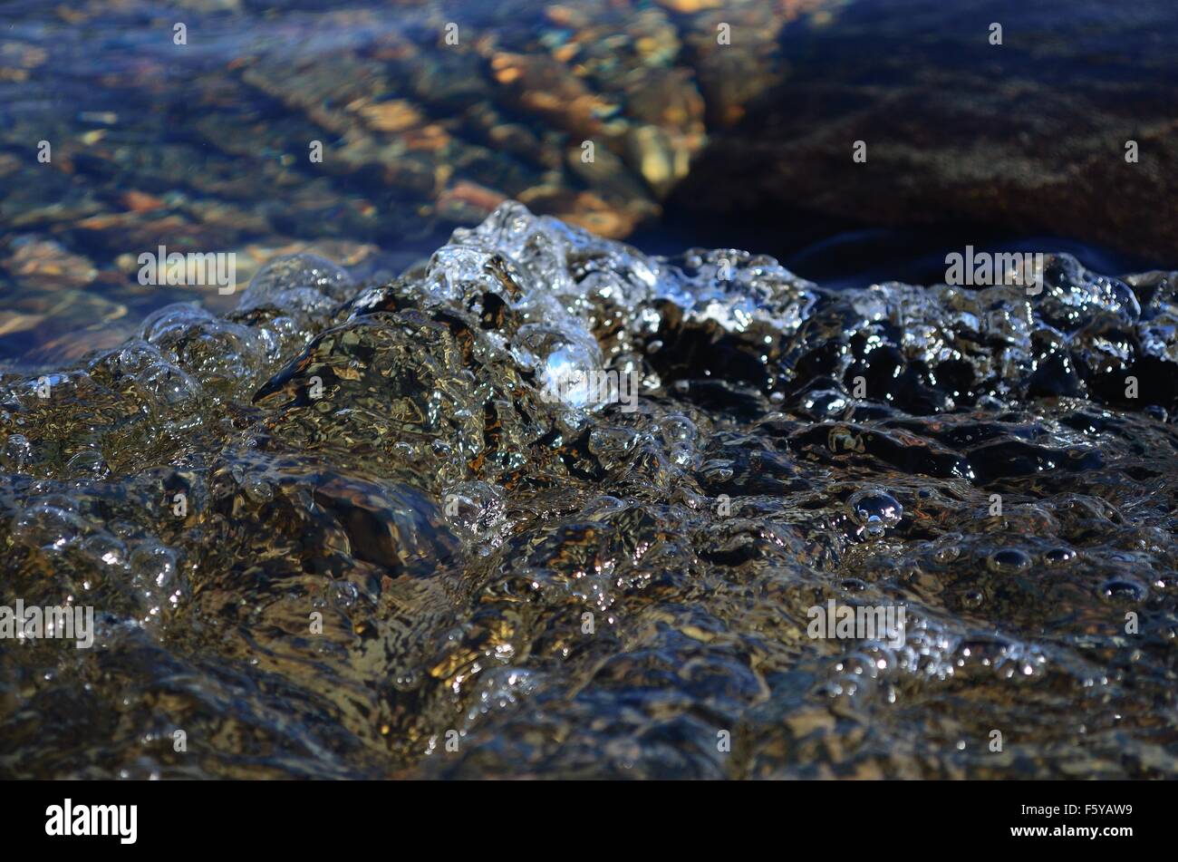 cold river water stream hit a black river rock in summer sunshine Stock ...