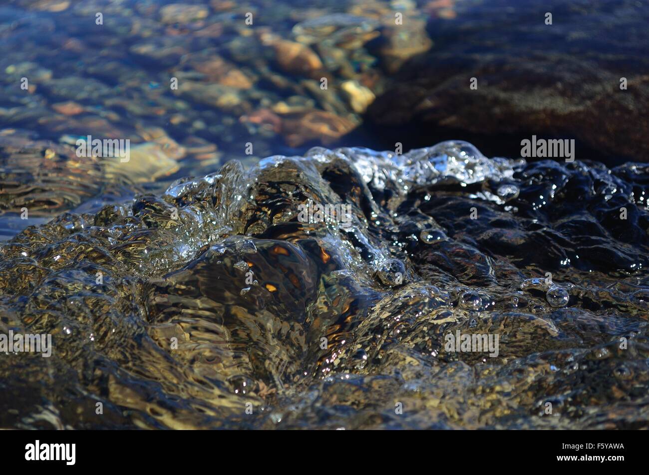 cold river water stream hit a black river rock in summer sunshine Stock ...