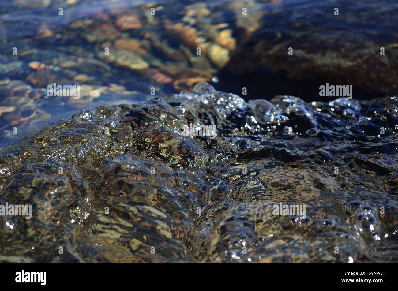 cold river water stream hit a black river rock in summer sunshine Stock ...