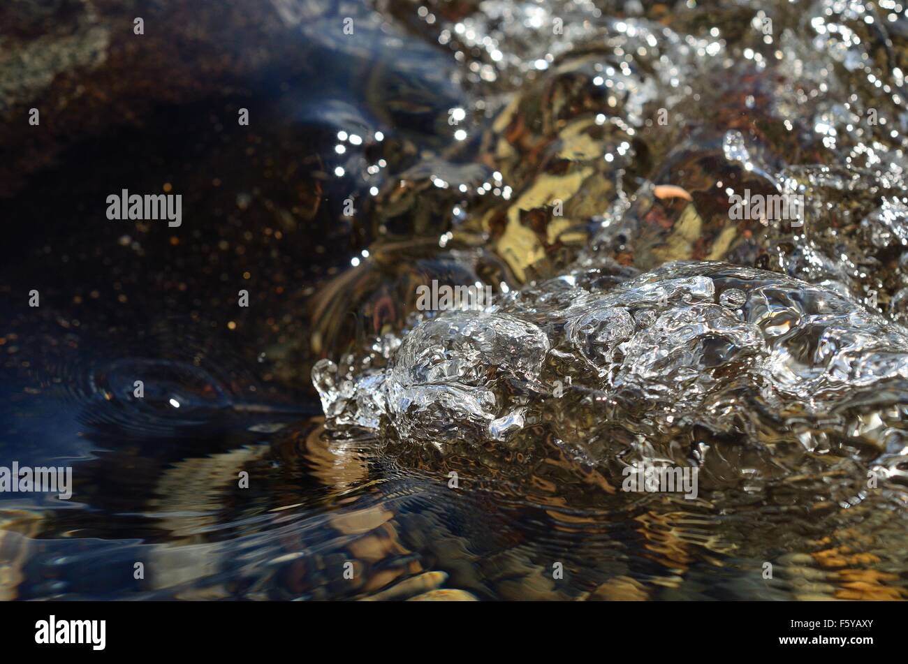 cold river water stream hit a black river rock in summer sunshine Stock ...