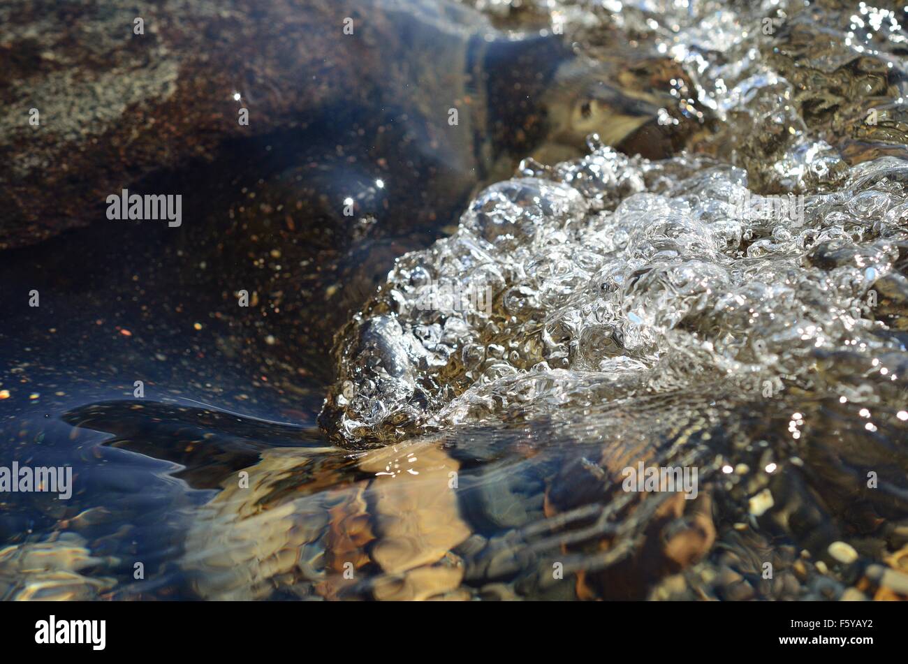 cold river water stream hit a black river rock in summer sunshine Stock ...
