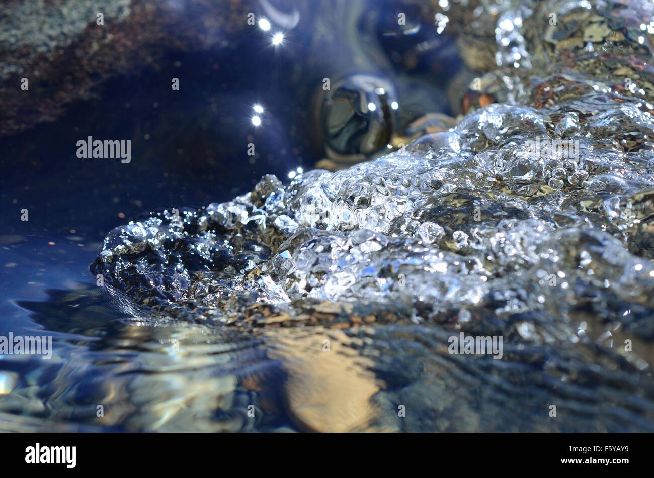 cold river water stream hit a black river rock in summer sunshine Stock ...