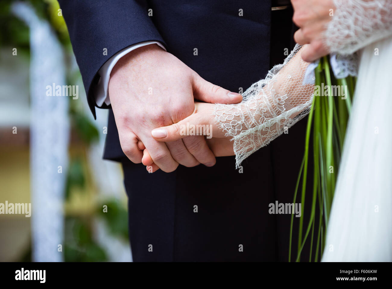 Bride and groom holding hands. The groom in a dark suit, the bride in a ...