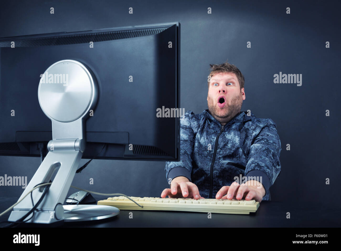 Surprised man sitting at desk looking at monitor screen Stock Photo - Alamy