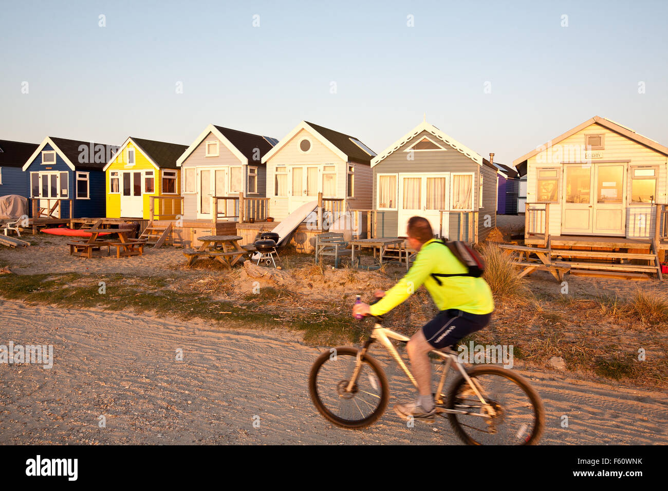 Cyclist on mountain bike passing at sundown, beach huts facing Christchurch Harbour with setting ...