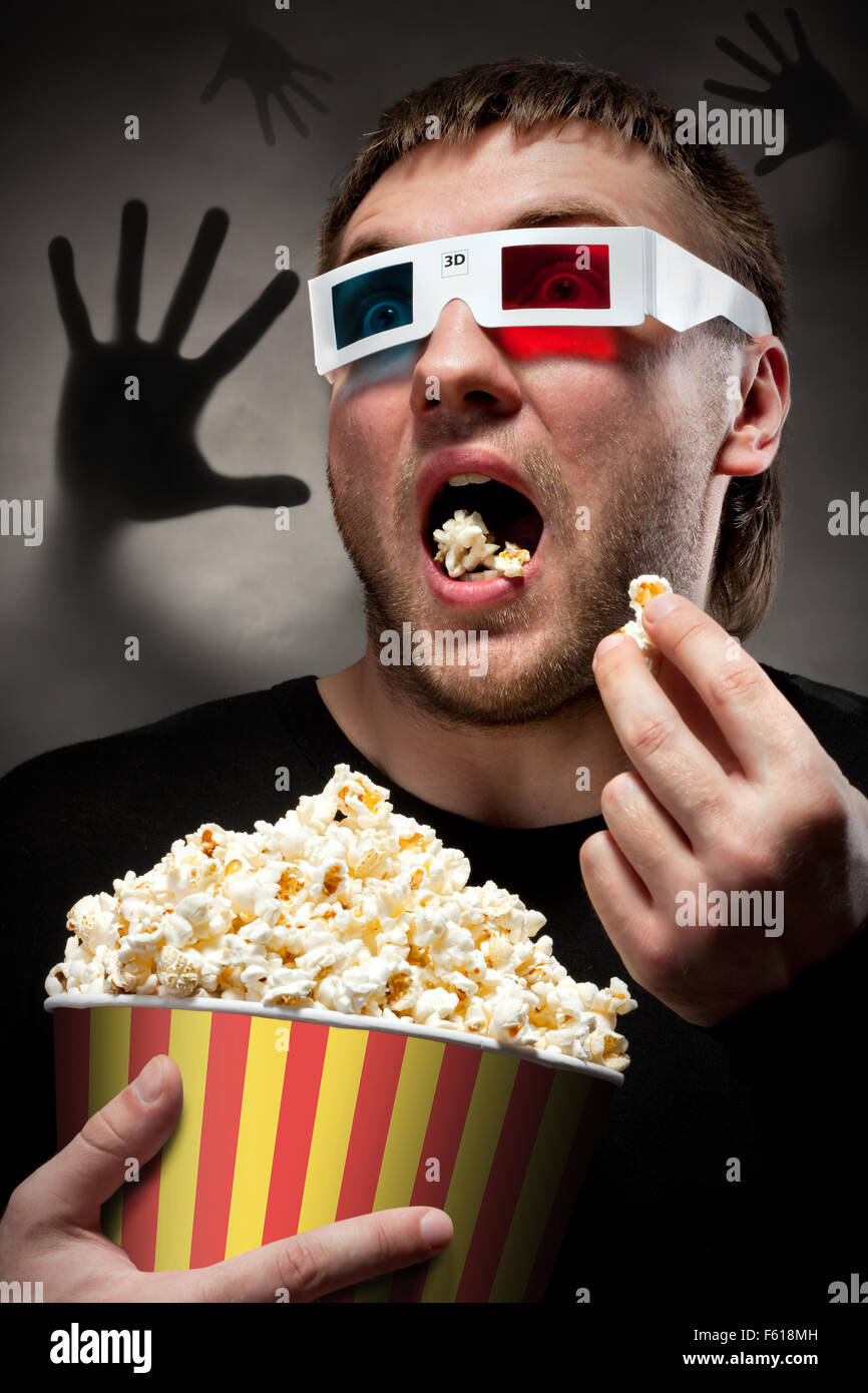 Portrait of scared man watching 3D movie and eating popcorn with dark ...