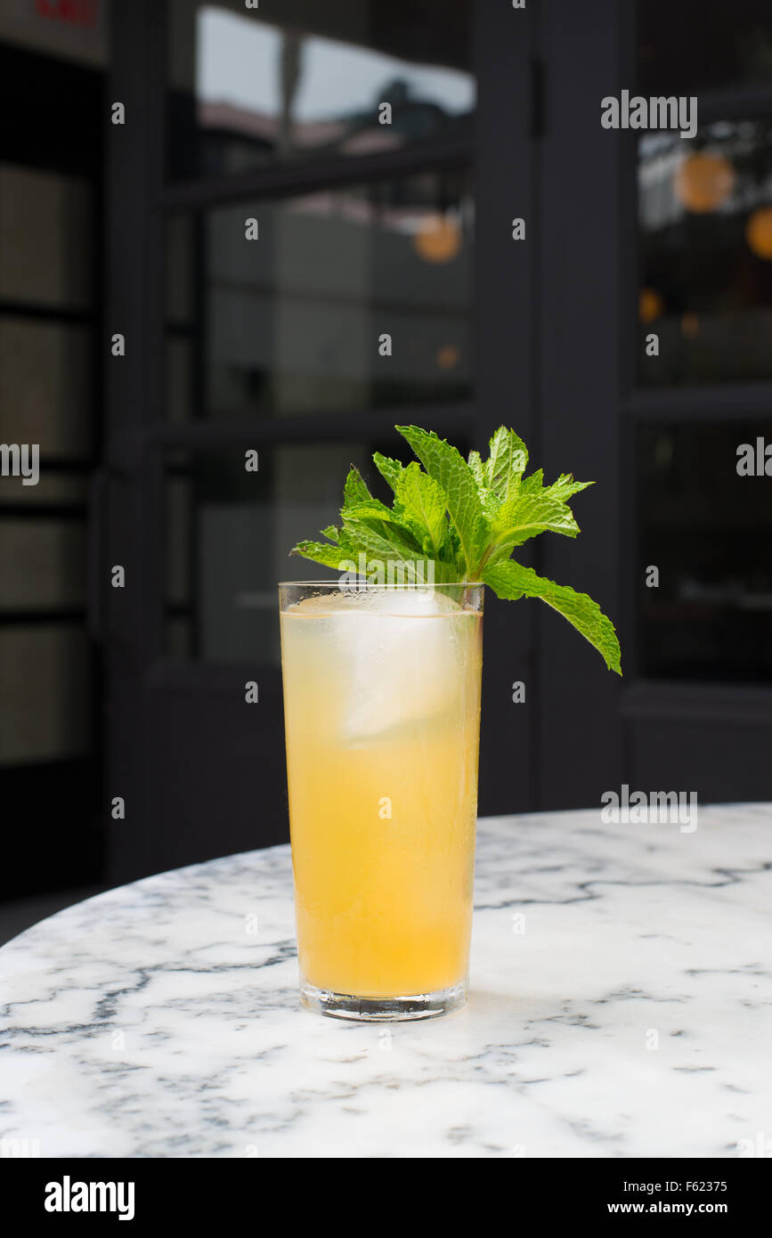 A bright yellow rum-based cocktail with a large mint garnish against a ...