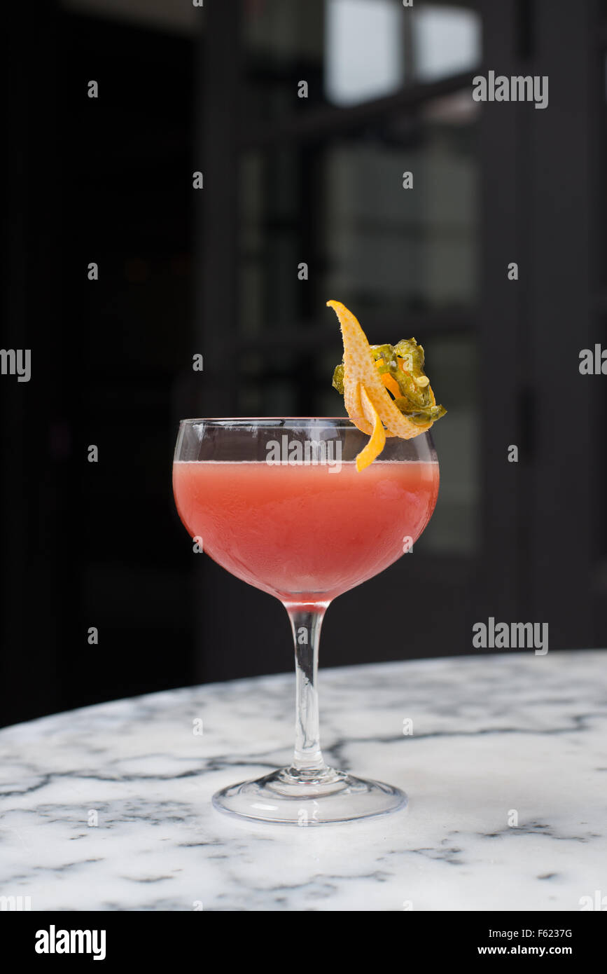 A light pink-colored mezcal cocktail with orange peel and jalapeno ...