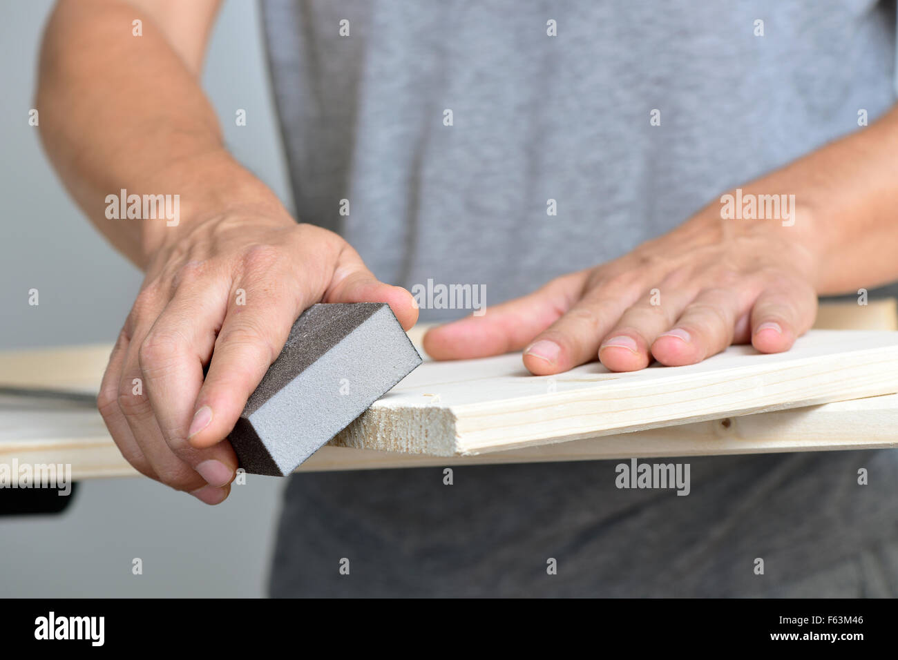 closeup of a young caucasian man sanding a wooden board with a sanding ...