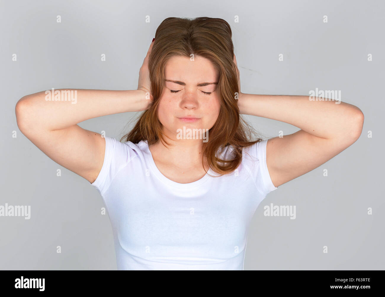 Too loud sound. Teenage girl covering ears with hands and keeping eyes ...